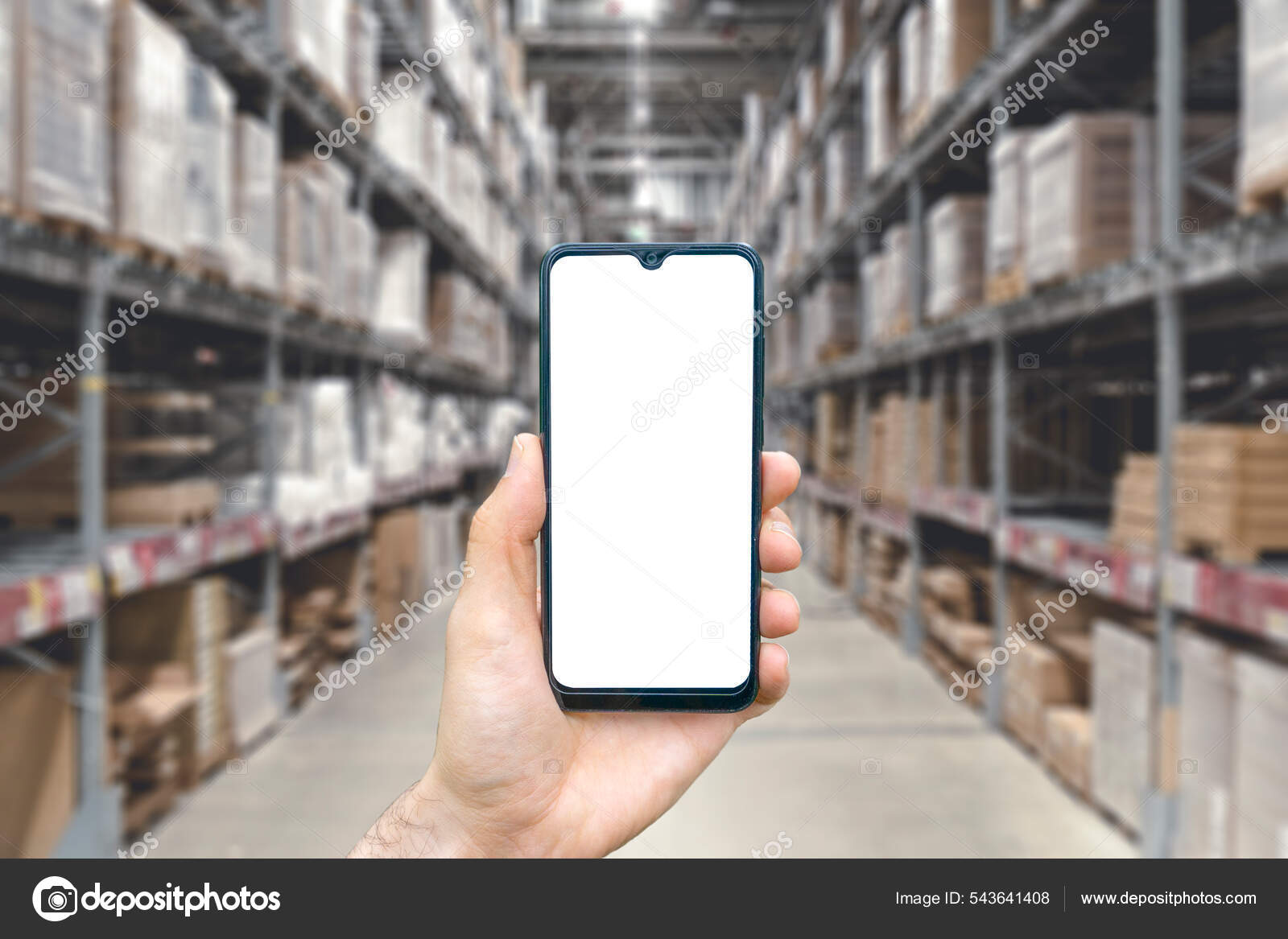 Warehouse with a hand holding an empty smartphone. Blurred industrial ...