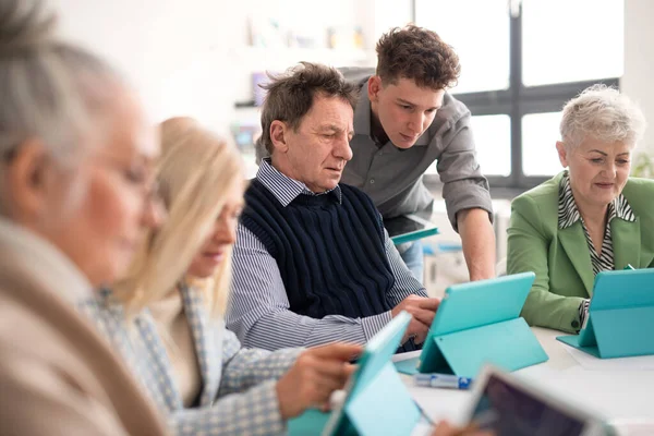 A group of seniors attending IT class in community centre with teacher ...