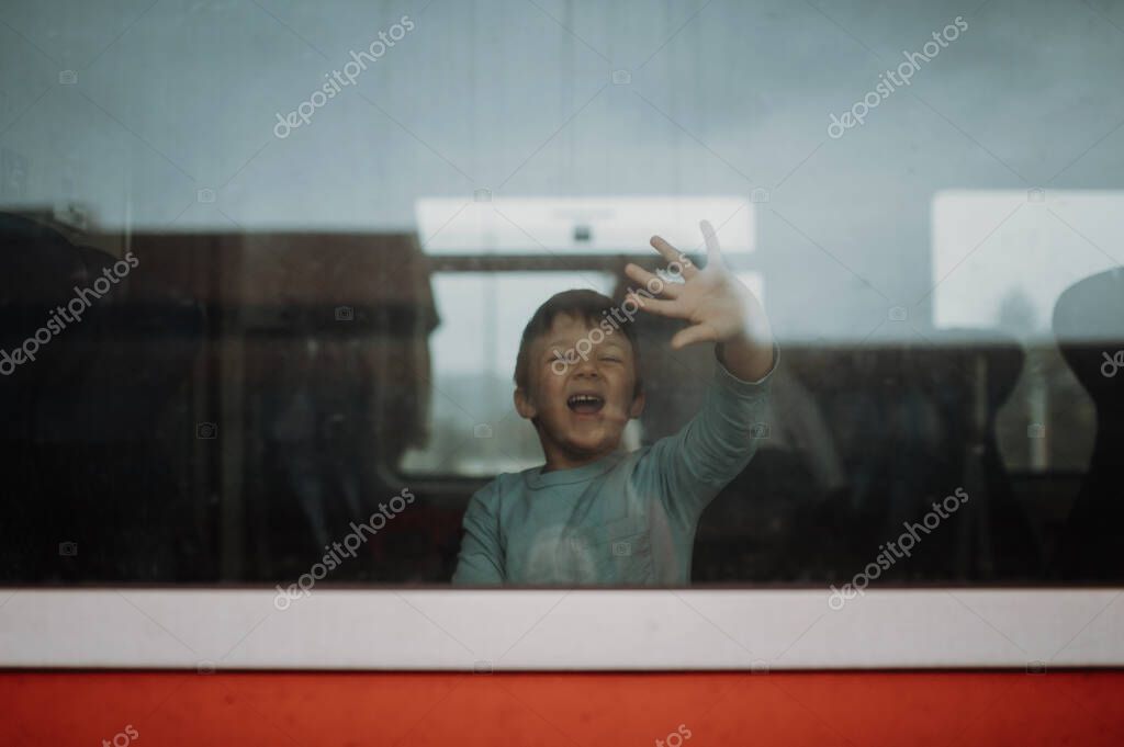 A happy little boy waving through window to say goodbye when travelling ...