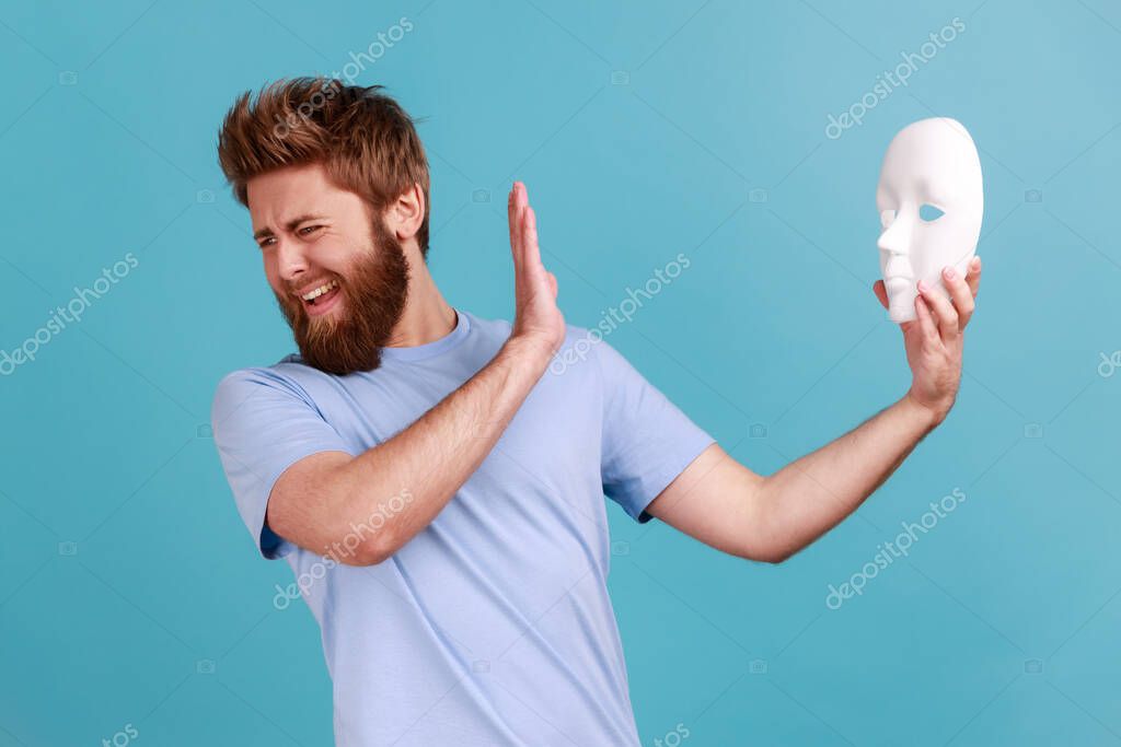 Portrait of scared bearded handsome man holding white mask and turning ...