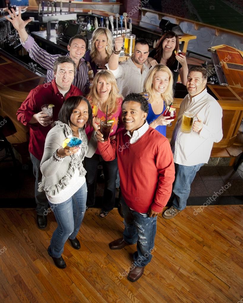 Adults enjoying a night out at a bar holding up drinks Stock Photo by ...
