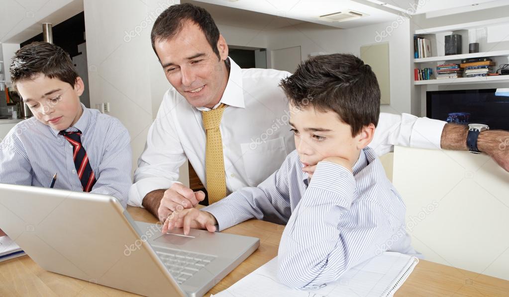 Father helping his two twin sons doing their homework using a laptop ...