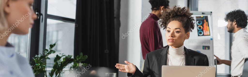 Mujer de negocios afroamericana señalando con la mano cerca de la computadora portátil y ...