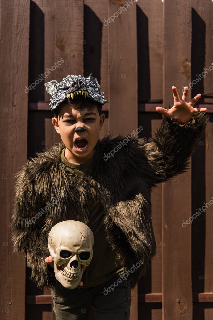 asiático chico en hombre lobo traje celebración cráneo mientras ...