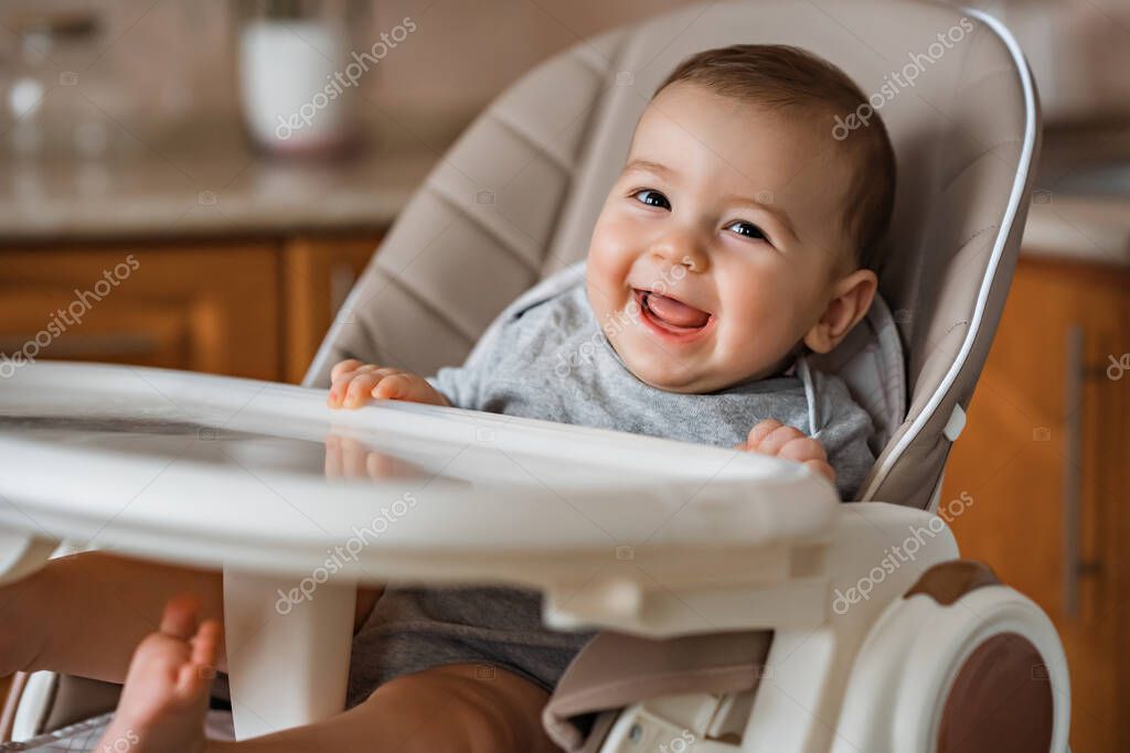Feliz bebé sentado en una silla alta en una cocina. Nutrición saludable ...