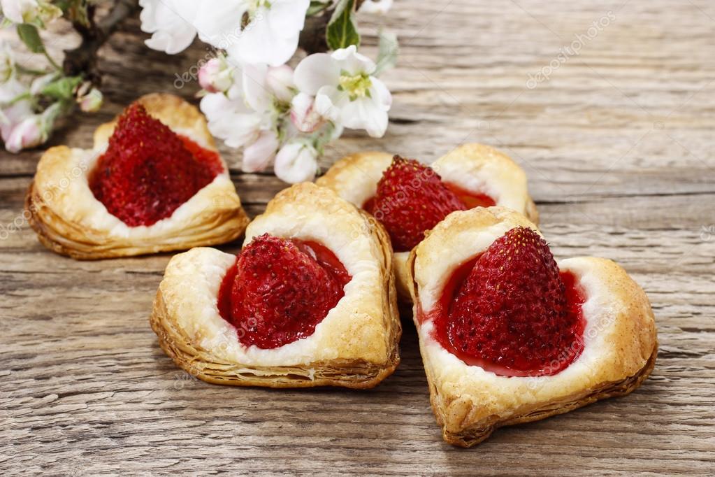 Puff pastry cookies in heart shape filled with strawberries. Blo ...