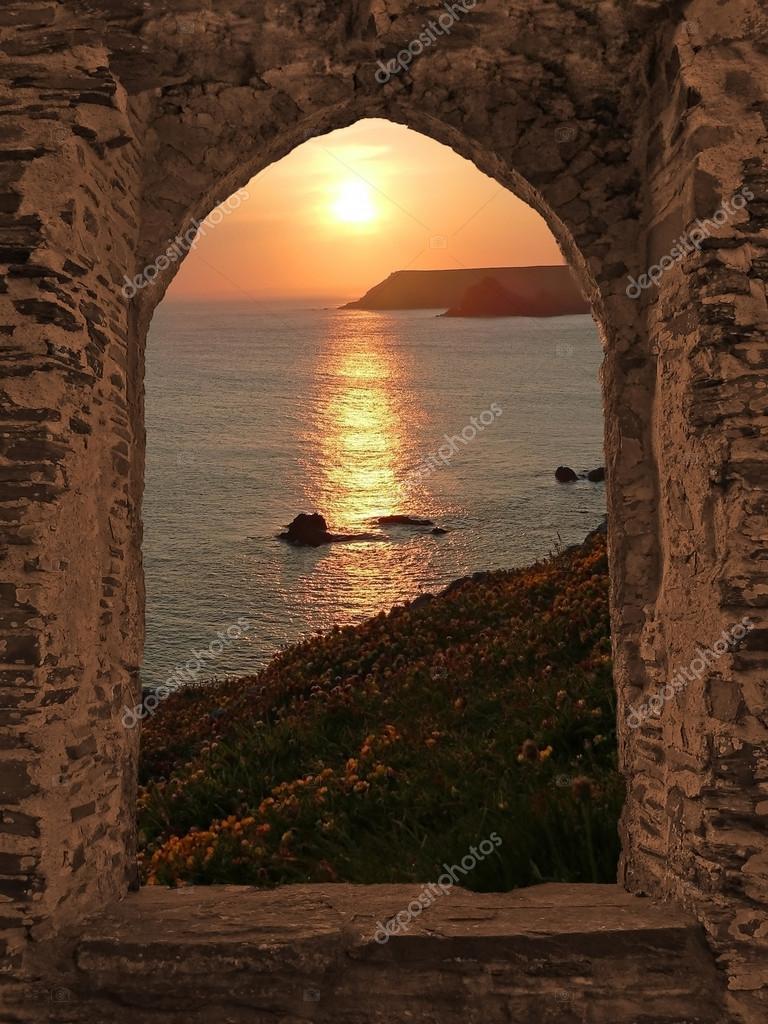 View through arched castle window to sunset coastal landscape, cornwall ...