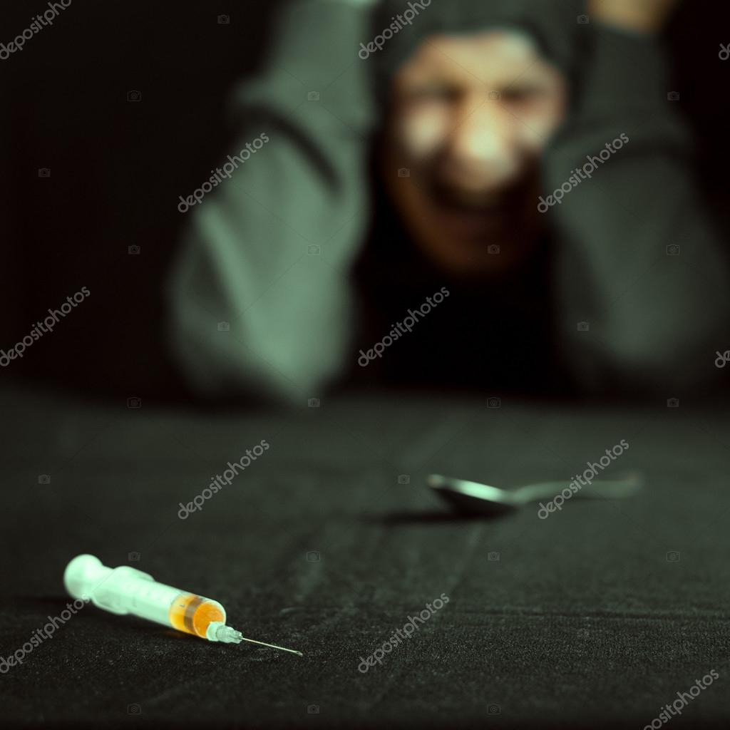 Grunge image of a depressed drug addict looking at a syringe and drugs ...