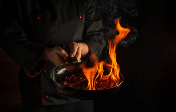 Professional chef prepares vegetable food in a frying pan with flame of ...