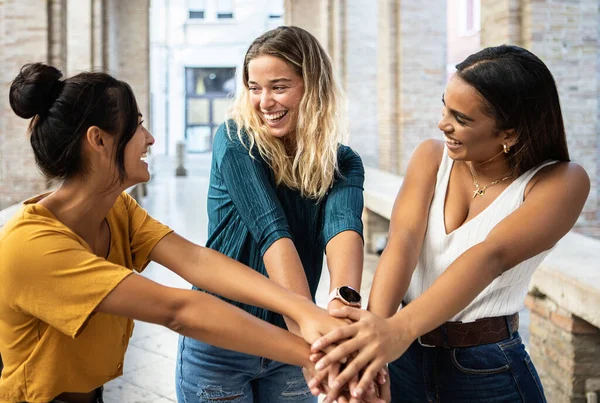 Three united multiethnic young women friends stacking hands outdoors ...