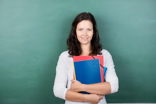 Teacher Holding Files Against Chalkboard - Stock Image - Everypixel