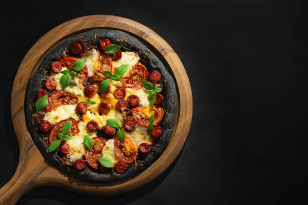 Pizza negra con tomates, salchichas, mozzarella y albahaca. Masa con ...
