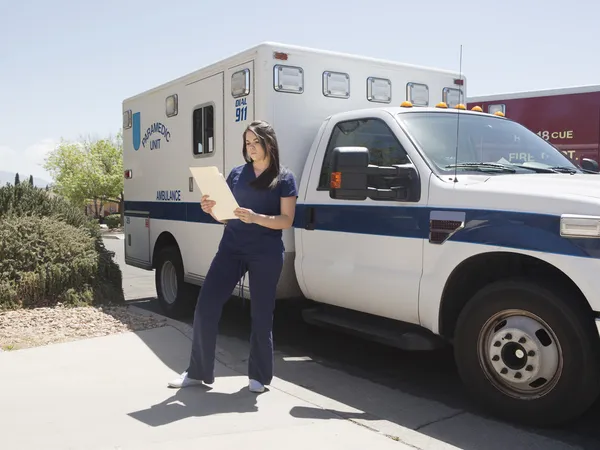 Nurse reviewing patient file standing next to ambulance and red fire ...