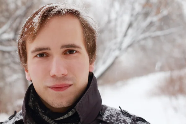 Young man with snowflakes in hair looks at camera at winter snow ...