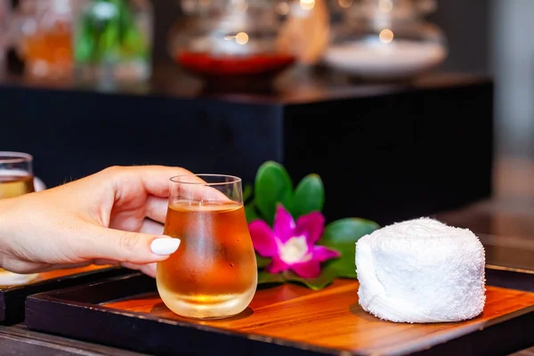 Woman hand take a herbal spa tea in a glass cup with small refreshment ...