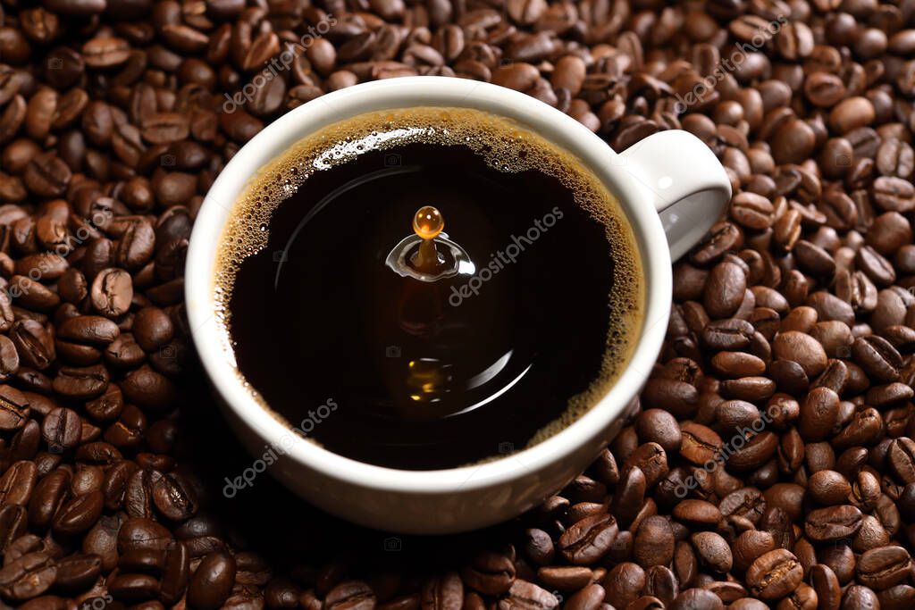 Drop of coffee falling into coffee cup sitting in a pile of freshly ...