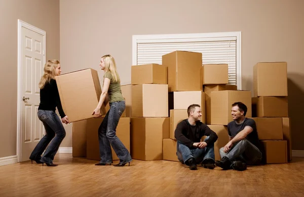 Two Women Carrying Boxes While Two Men Sit - Stock Image - Everypixel
