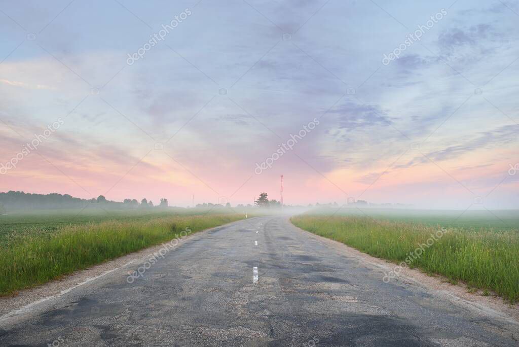 Carretera de campo (antigua carretera asfaltada) a través del campo y el bosque al amanecer. Luz ...