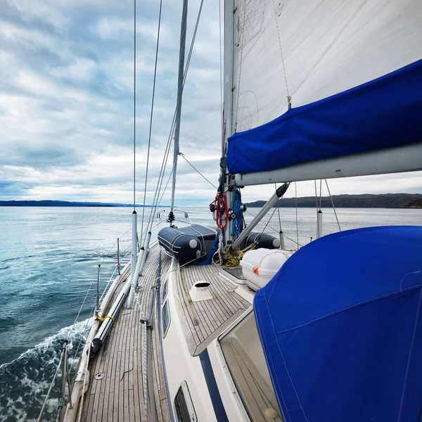 Wooden sloop rigged yacht sailing on a cloudy day, a view from the deck ...