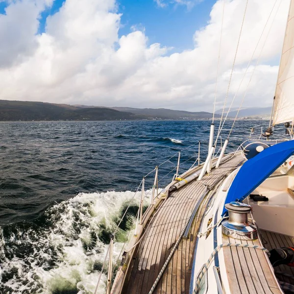 Sloop rigged modern yacht with wooden teak deck sailing near the rocky ...