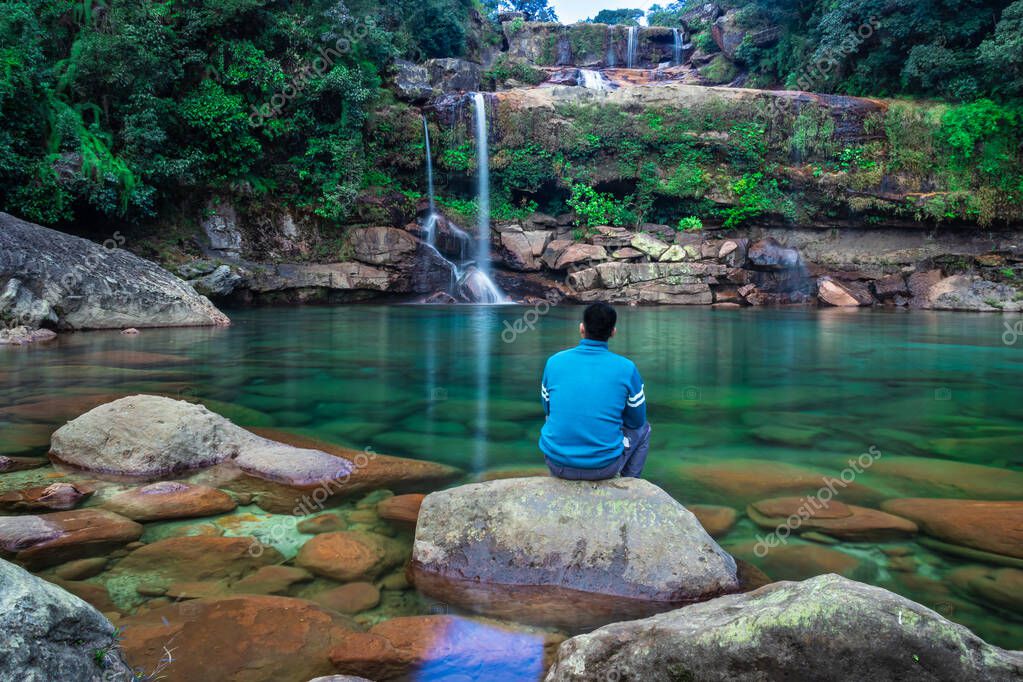 joven aislado sentado en la roca con fondo de cascada prístina en la ...