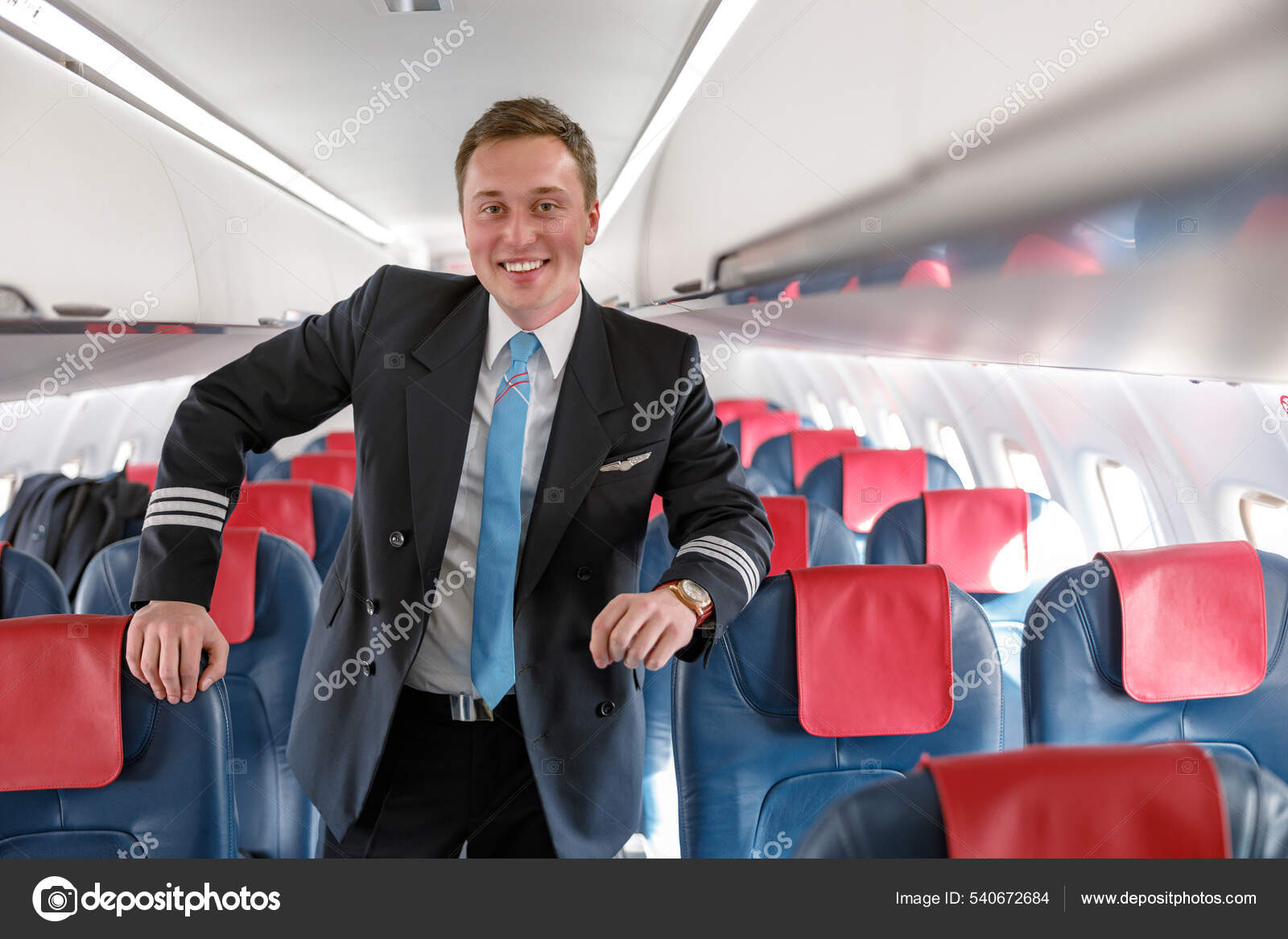 Cheerful male flight attendant standing in passenger airplane cabin ...