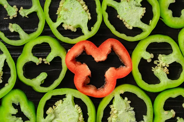 Green and red sweet pepper cut into rings on a black wooden table or ...