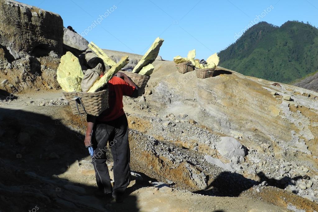 Trabajador minero de azufre en un volcán llevando trozos en una canasta ...