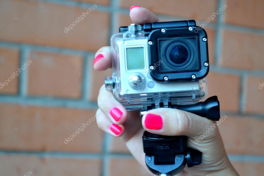 Hand with bright pink nails holding small camera in waterproof covering ...