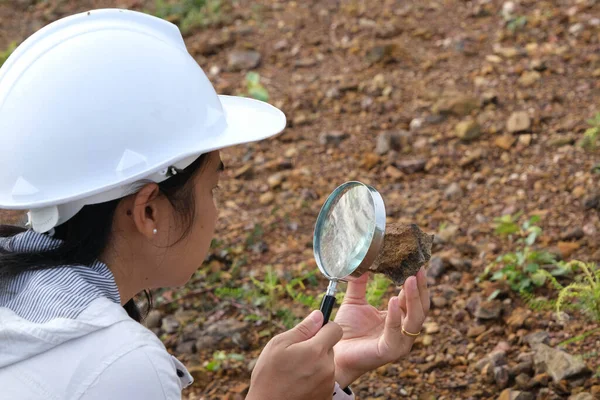 Female geologist using a magnifying glass examines nature, analyzing rocks or pebbles ...