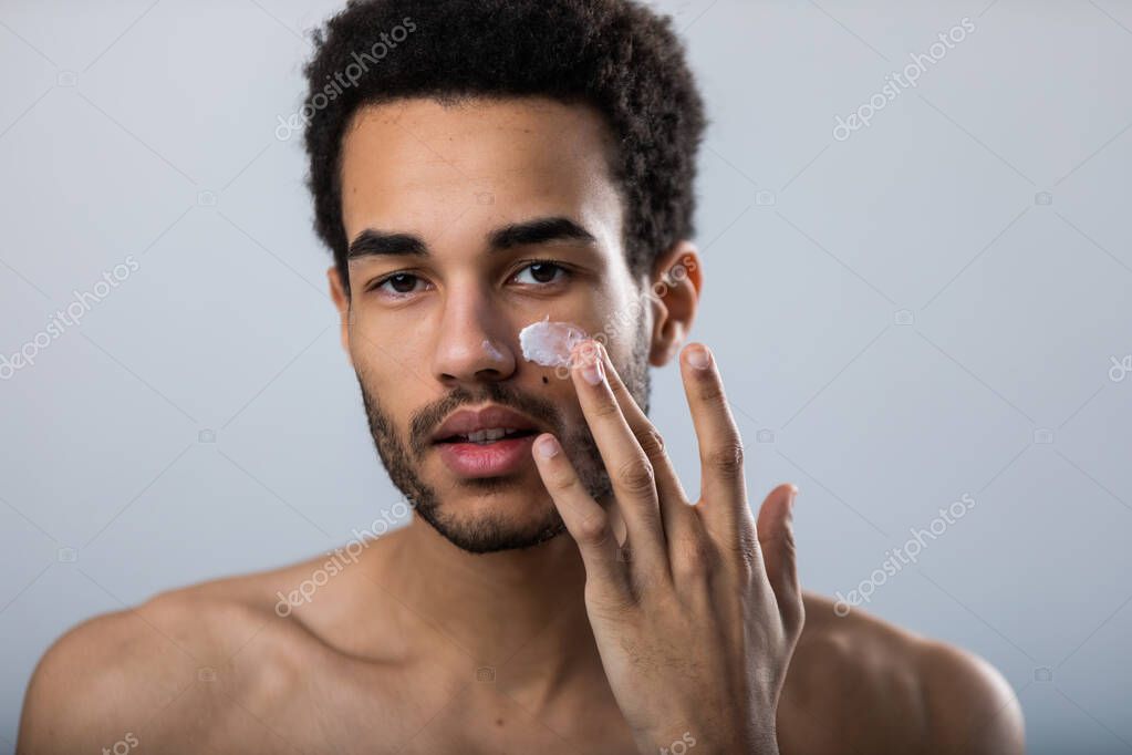 El joven afroamericano se aplica crema hidratante en la cara. Cuidado ...