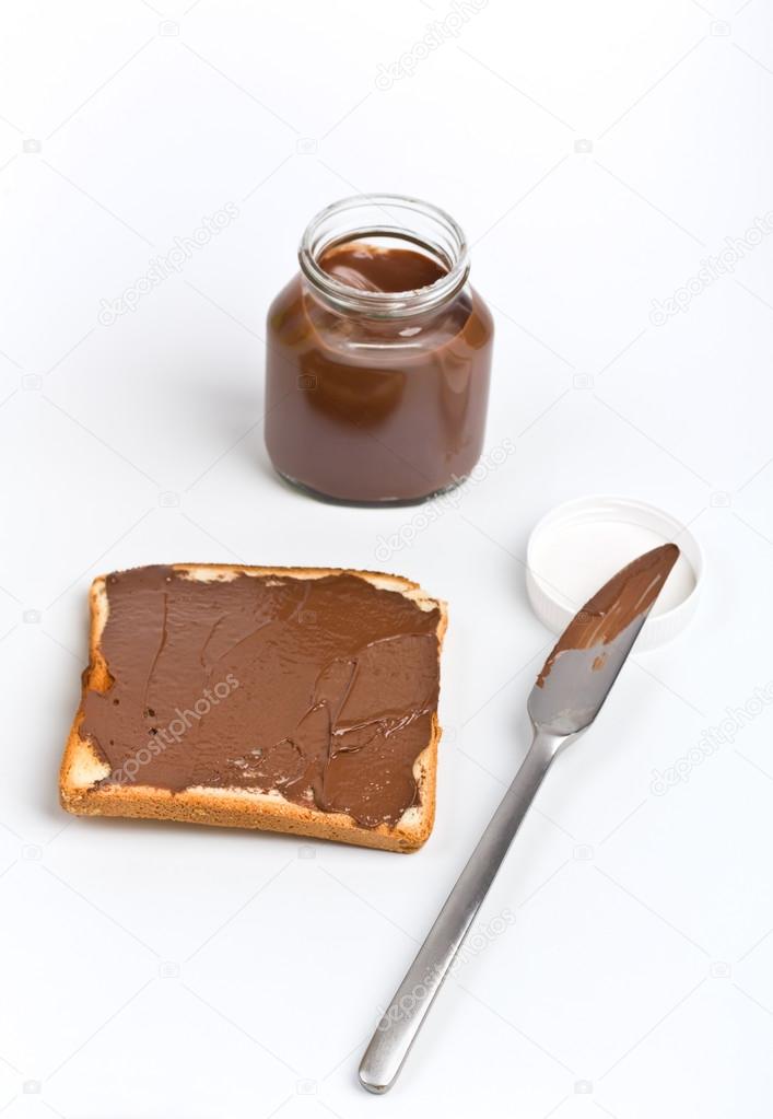 Open chocolate spread container with a buttered toast and a knif ...