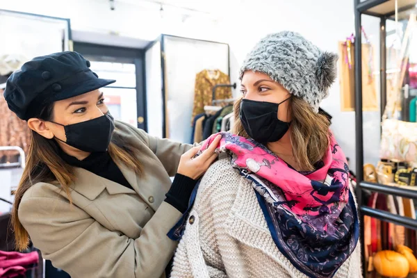 An employee with a mask from a clothing store testing a pink scarf on a ...