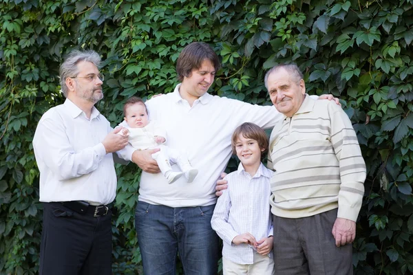 Four generations of one family sitting at a wooden table in the garden ...