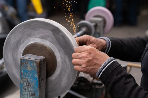 Man holding in hands axe closeup and using sharpening machine. Senior ...