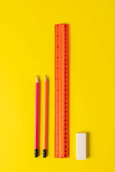Vertical composition of rulers, pencils and eraser on yellow surface ...