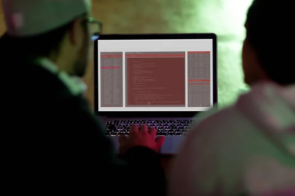 Back view of two diverse male colleagues at desk using computer with coding on screen. coding ...