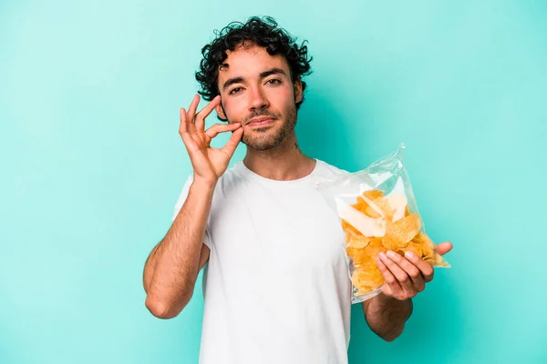 Young caucasian man holding a bag of chips isolated on blue background ...