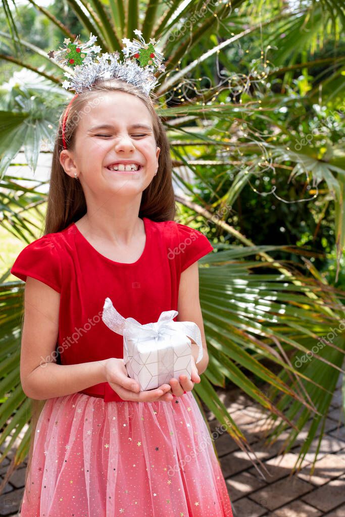 Una linda chica hermosa en un vestido rojo se encuentra cerca de una palmera, tiene un regalo en ...