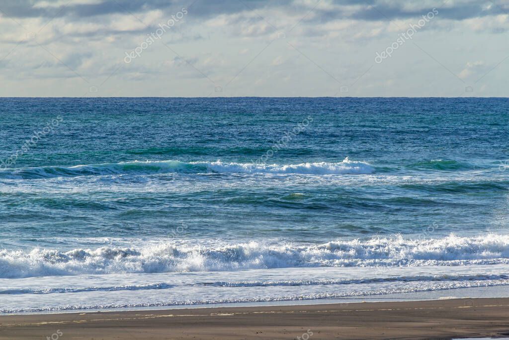 Ondas onduladas, arena negra y vegetación verde brillante resaltan una ...
