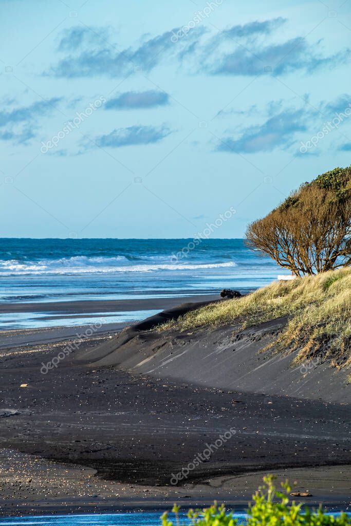 Ondas onduladas, arena negra y vegetación verde brillante resaltan una ...