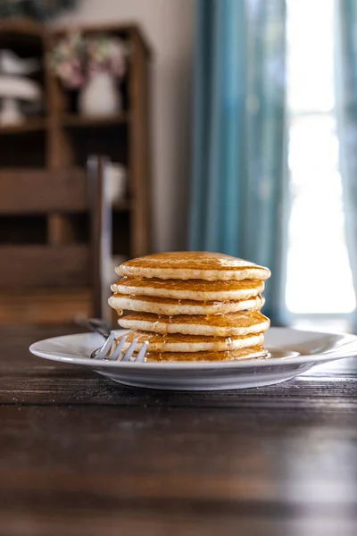 A plate with a stack of plain homemade pancakes at a dark wood kitchen ...