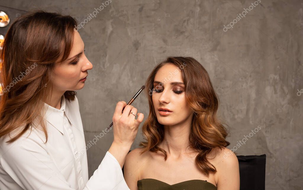 primer plano de un artista de maquillaje experto pinta los ojos de una chica modelo sobre un ...