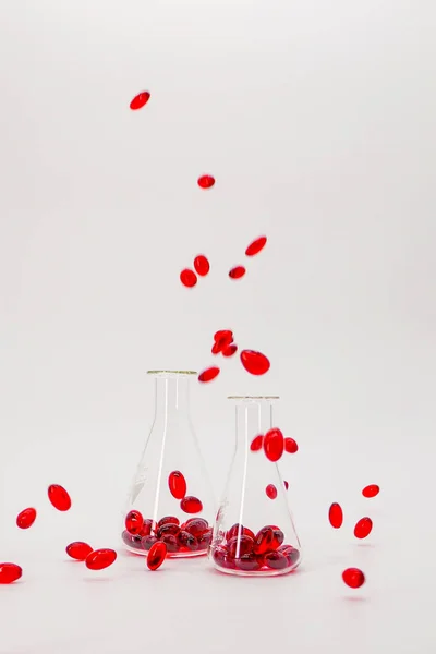 Krill oil red capsules in laboratory transparent flasks on a white ...