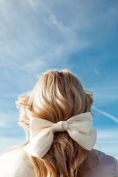 Back view of woman with long wavy fair hair decorated with beige bow ...