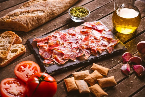 Jamón ibérico cortado en un plato de pizarra sobre una mesa de madera ...