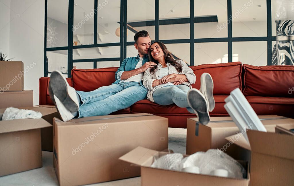 Pareja casada joven sentada en un sofá abrazándose en la sala de estar ...