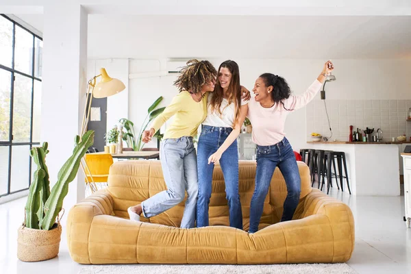 Three funny female friends dancing and singing on the sofa at home ...