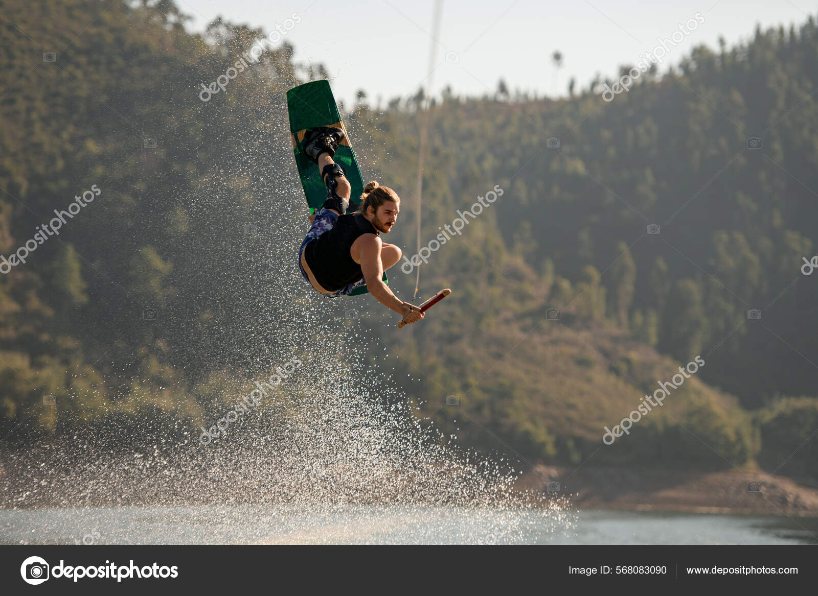 Active male rider holds rope and making extreme jump on wakeboard ...