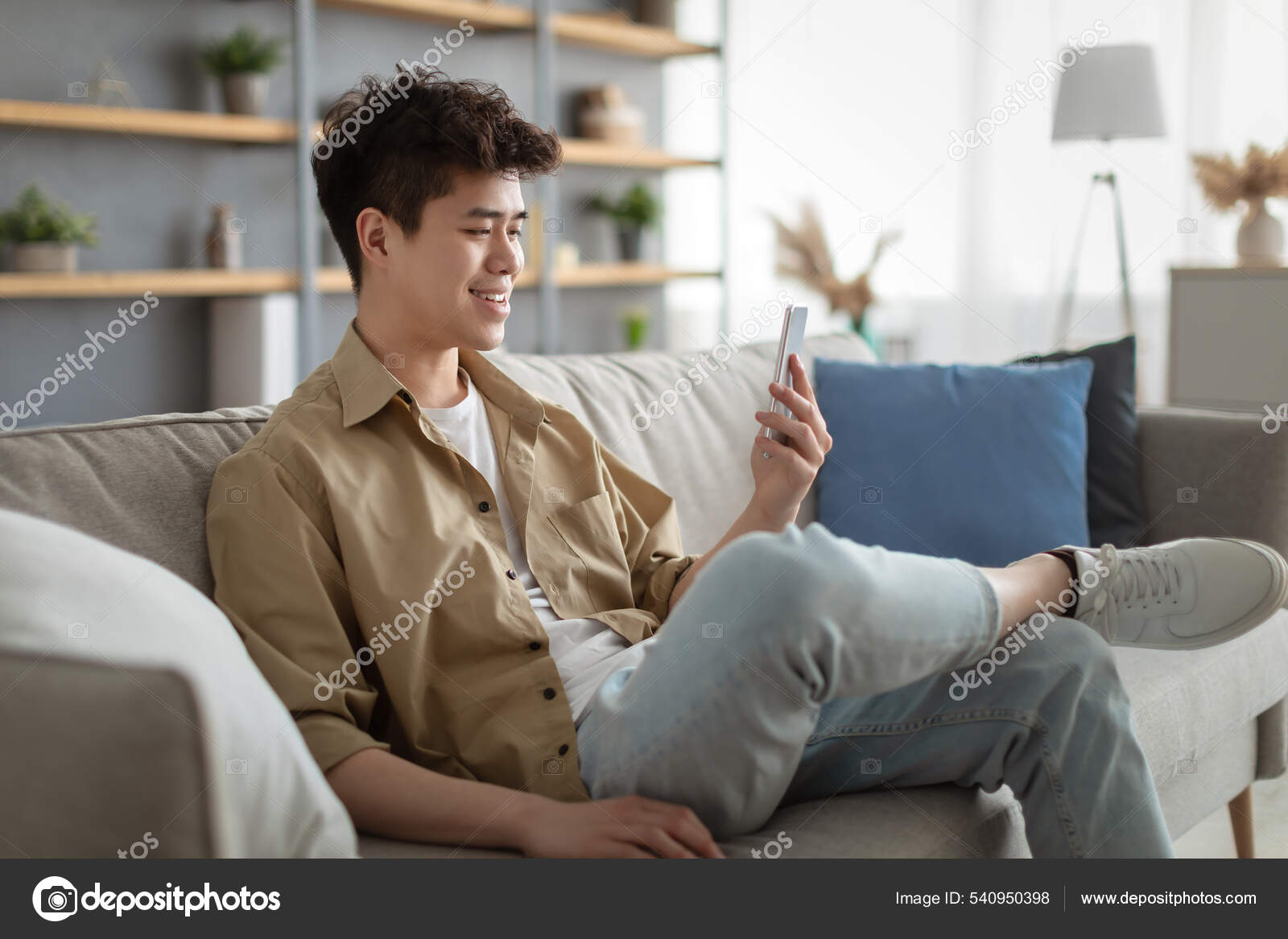 Smiling asian man using smartphone at home sitting on couch — Stock ...